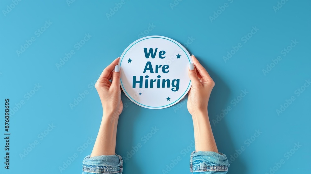 We Are Hiring sign held by two hands against a clean, solid pastel blue ...