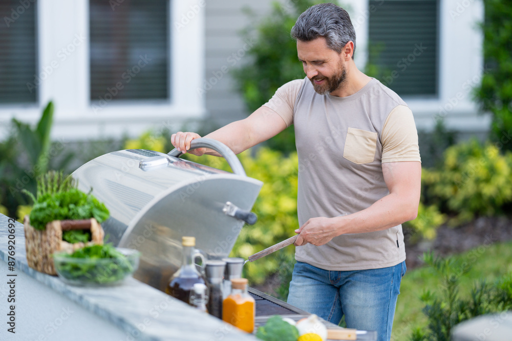 Handsome smiling hispanic man making barbecue at backyard. Picnic barbecue party. Chief cook ...