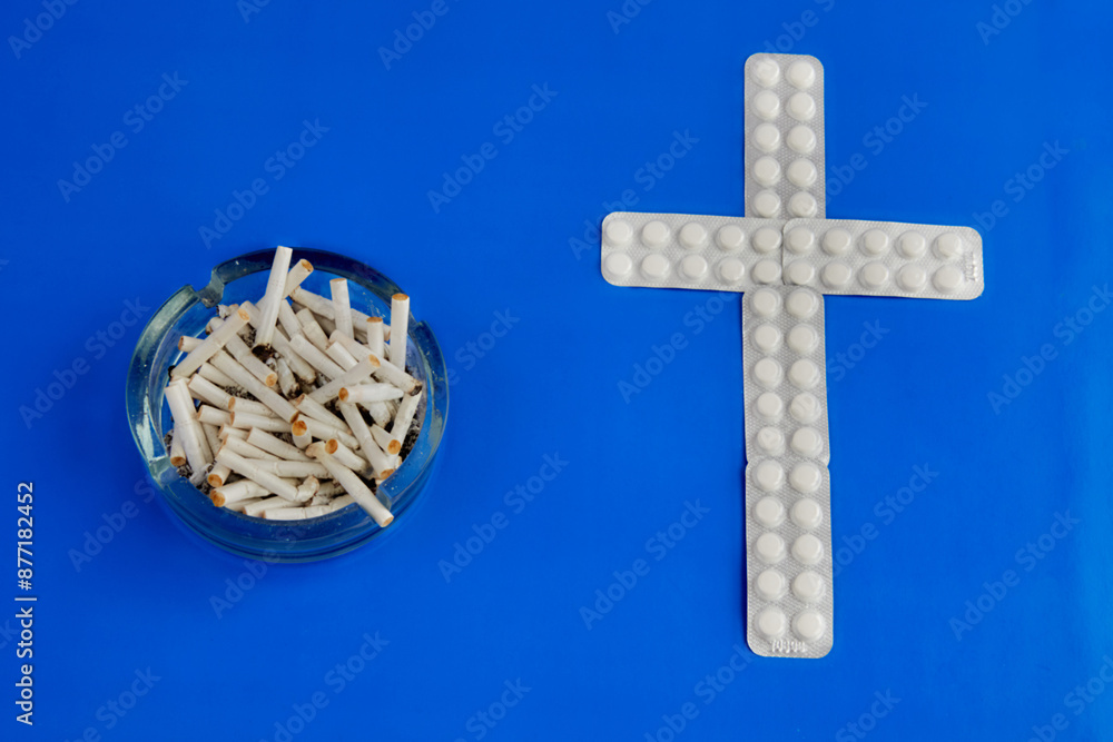 Ashtray with cigarette butts and next to it a cross of blister packs of ...