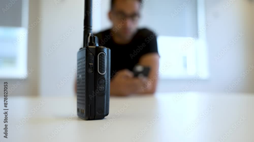 A two-way radio placed on a white table with a blurred person holding a ...