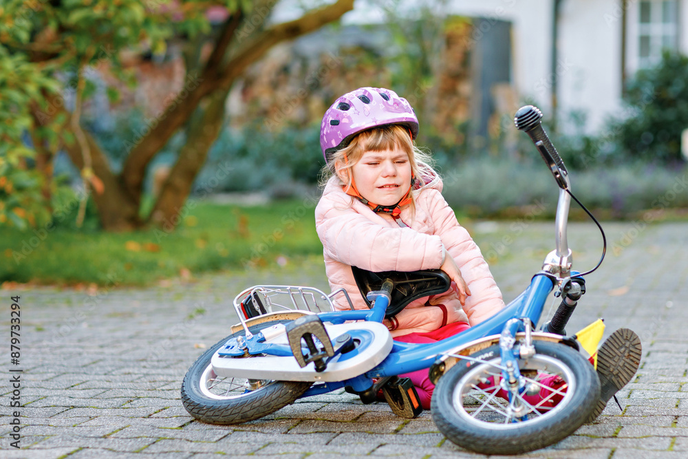 Cute little girl sitting on the ground after falling off her bike ...
