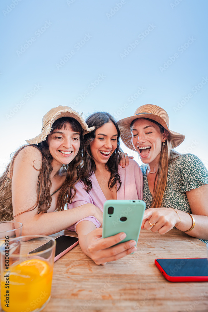 Vertical. Three girls watching the smartphone on a shore bar terrace ...
