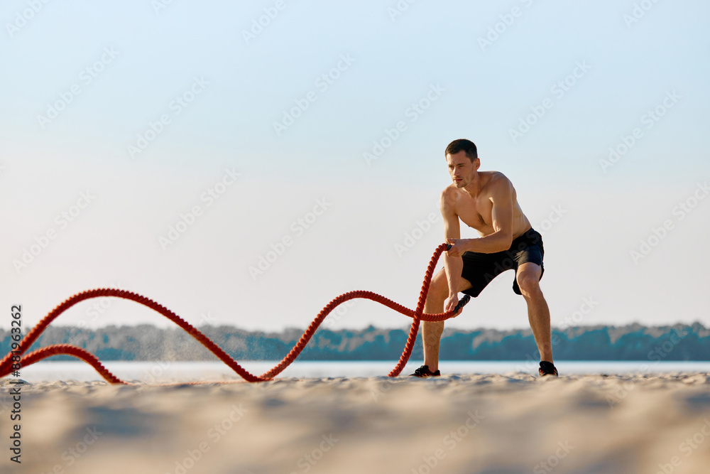 Shirtless man in black shorts using red battle ropes for workout on ...