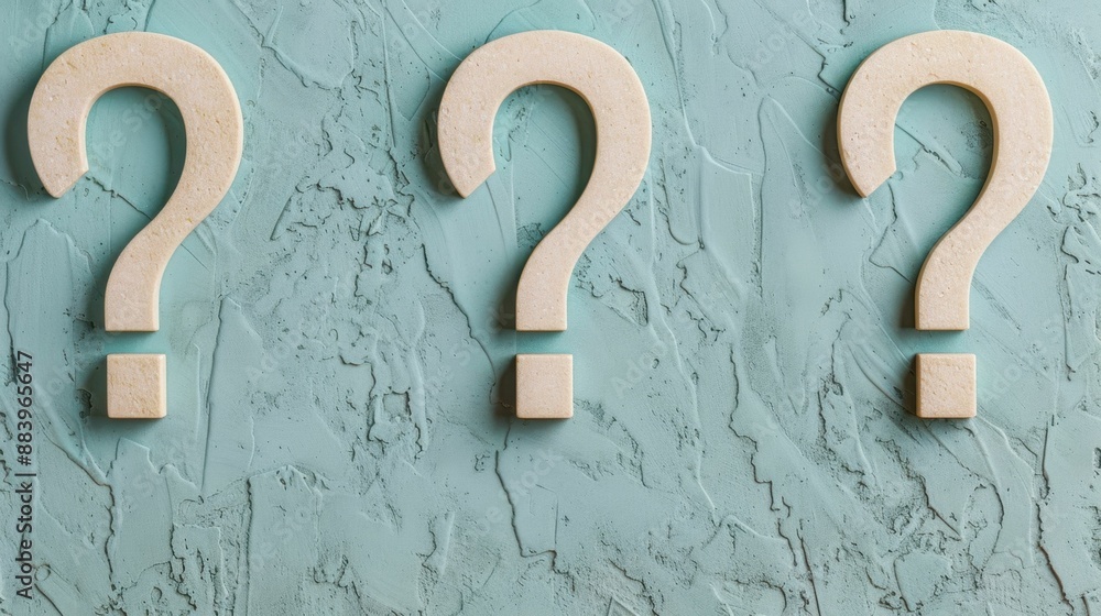 Three wooden question marks on a textured teal background symbolizing ...
