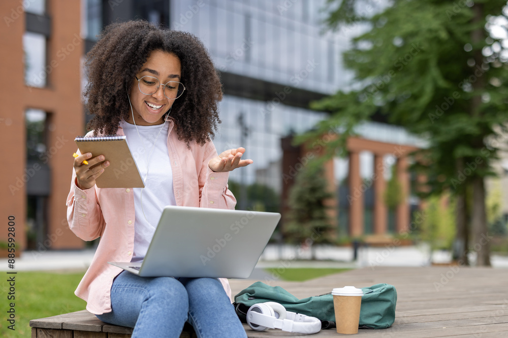 Woman student sitting outside university campus using laptop, taking ...