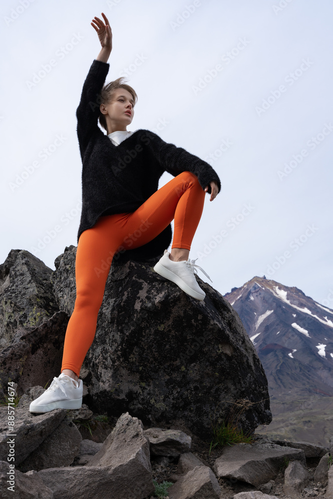 Woman tourist sitting with one arm raised high above head on rocky ...