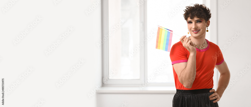 Young transgender woman with LGBT flag near window at home. Banner for ...