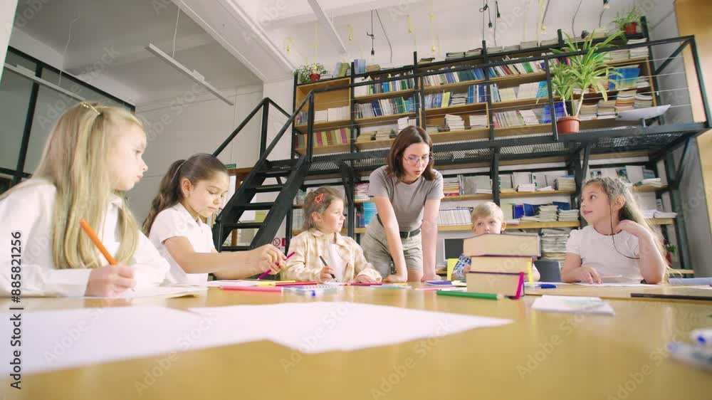 Elementary school students sit at a round table in an art class, and a ...