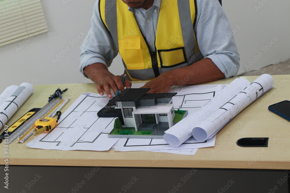 An engineer meticulously draws house plans on a workbench, surrounded ...