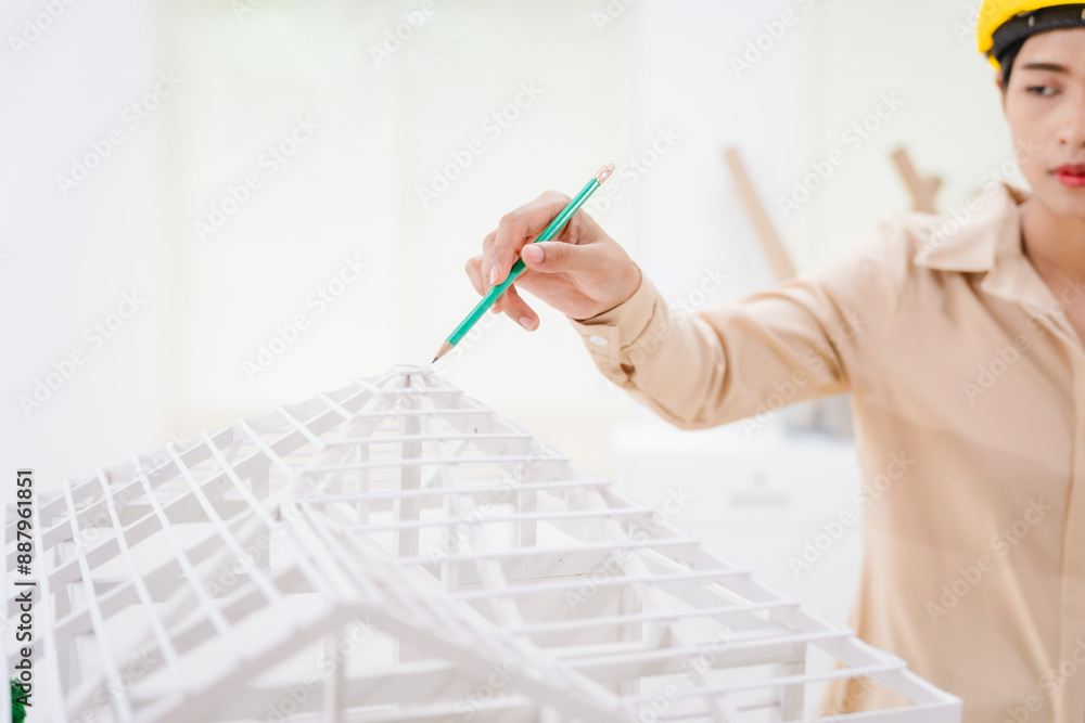 An Asian architect woman sits at her desk, wearing a yellow safety hat ...