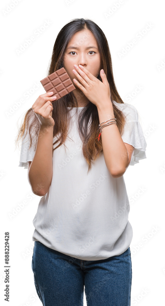 Young asian woman eating chocolate bar over isolated background cover ...