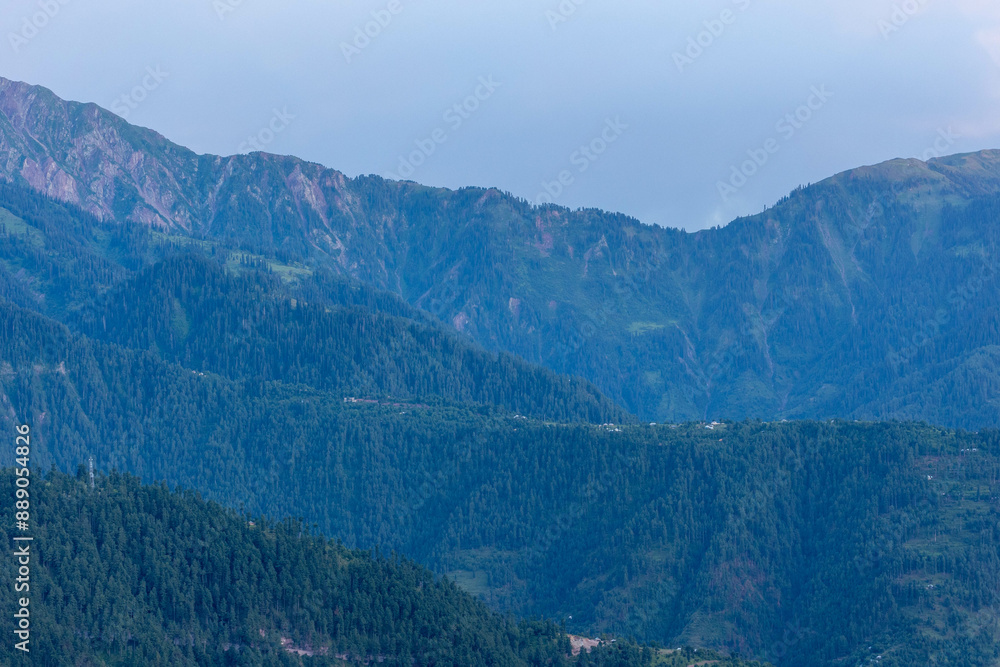 Vast mountain range covered by a green forest with a small village in ...