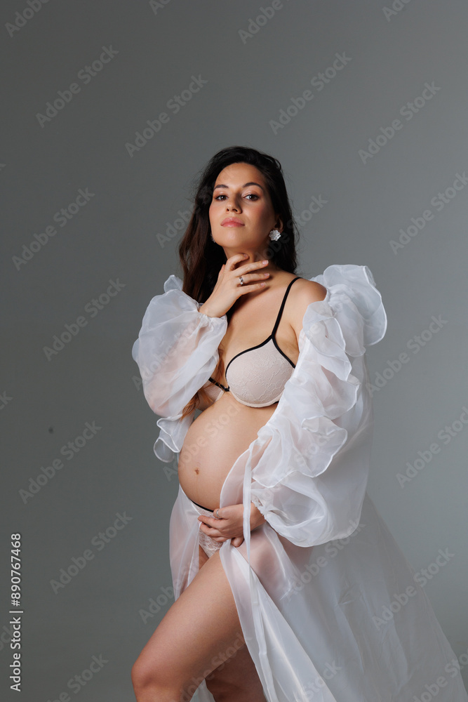 A beautiful pregnant brunette woman in a white flying transparent negligee, dressing gown. A ...
