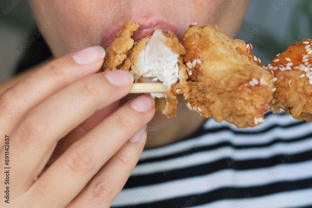 Person eating fried chicken on a skewer, topped with sesame seeds ...