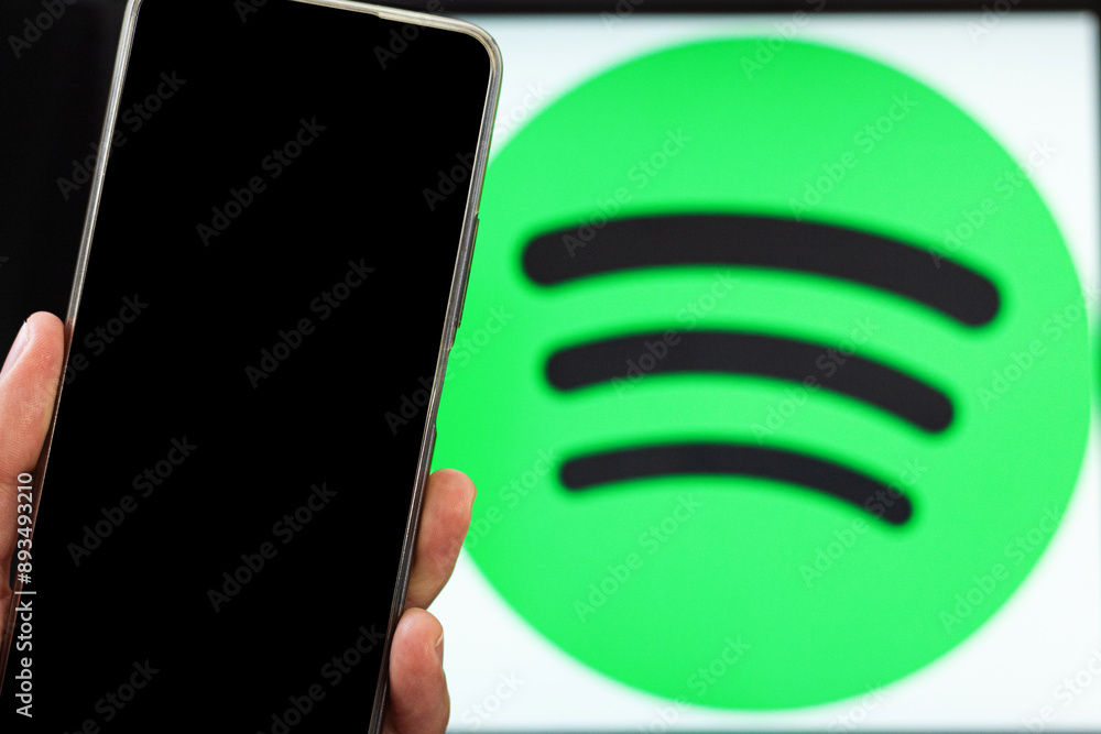Hand holding a cell phone with black screen over the Spotify logo ...
