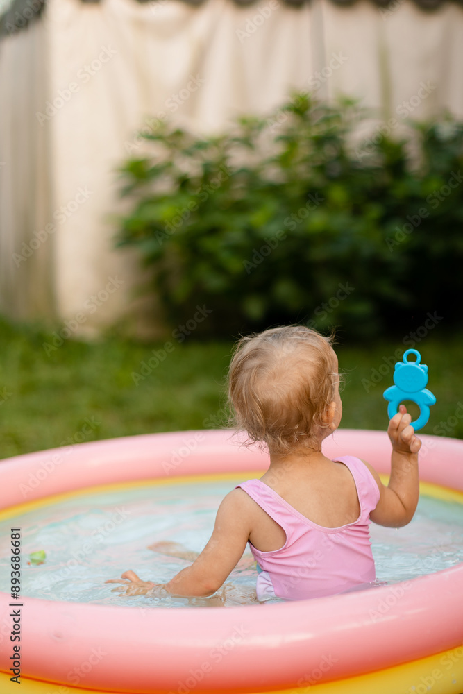 Baby in a pink swimsuit is swimming and playing with toy in inflatable ...