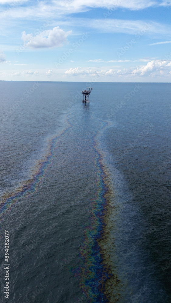 An oil sheen flows in the water during a spill from an offshore ...