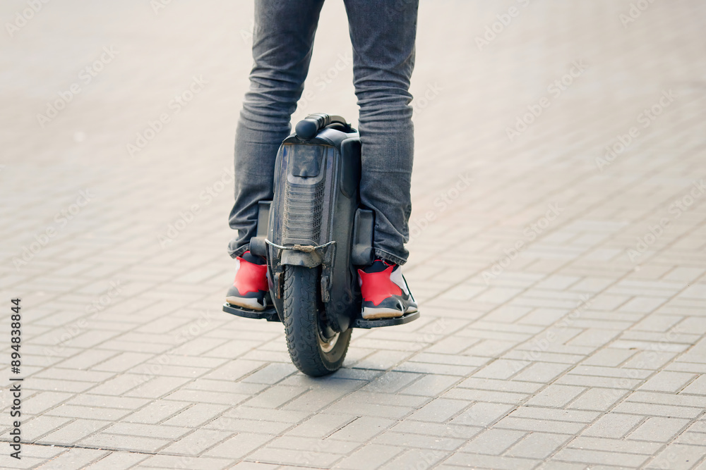 Man on electric wheel riding on sidewalk closeup. Rider's legs on an ...