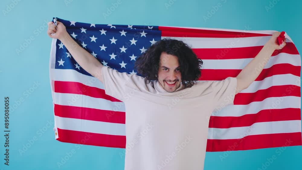 A young man with curly hair happily poses with an American flag ...