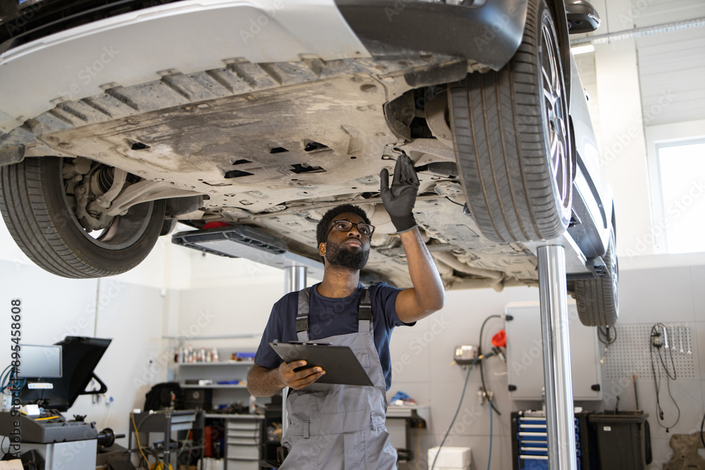 Mechanic conducts vehicle inspection while car is elevated on hydraulic ...