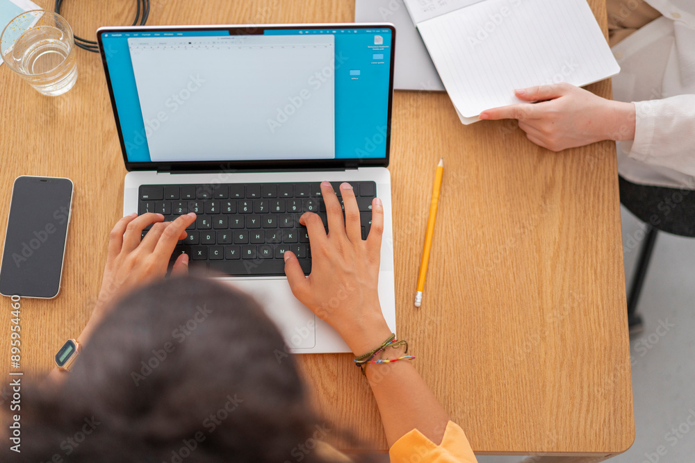 A young professional typing on a laptop while analyzing charts and ...