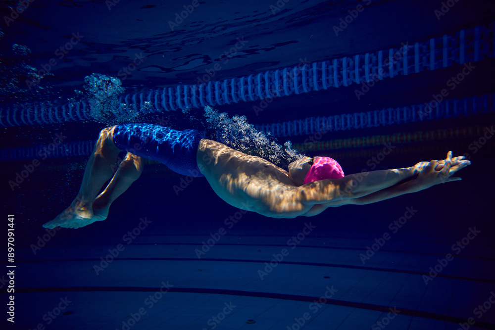 Male swimmer, wearing pink cap and blue trunks, in training shows his ...