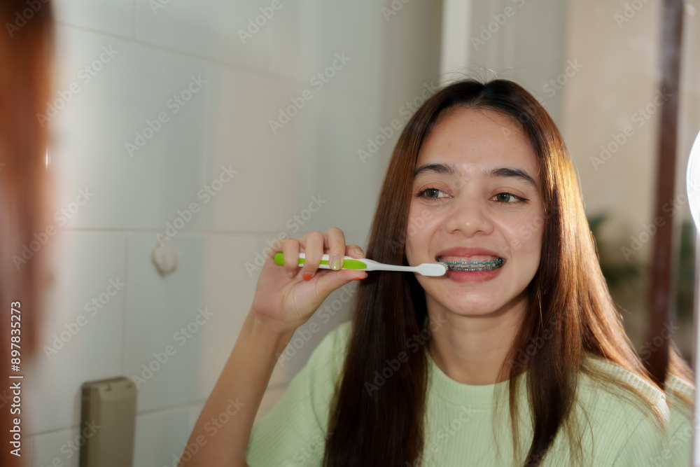 Asian teenage girl brushing teeth with braces in bathroom. Long ...