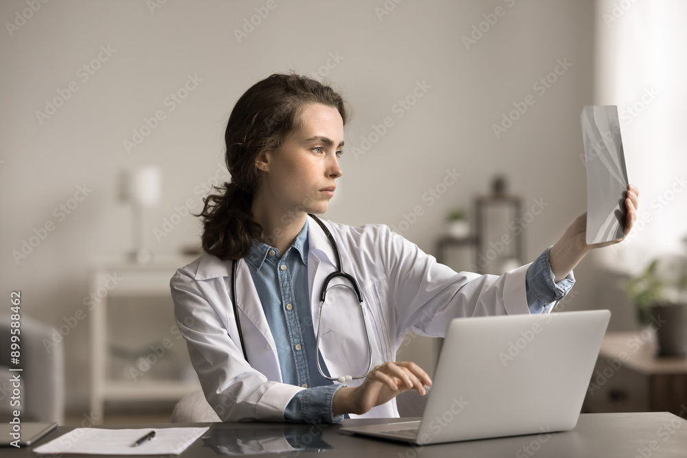 Female internist doctor sits at desk with laptop, holding X-ray results ...
