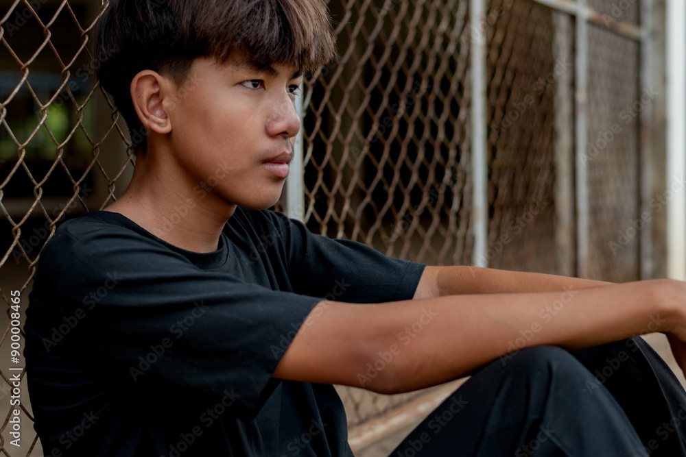 Asian teenboy in a black shirt sits with his knees pressed against a ...