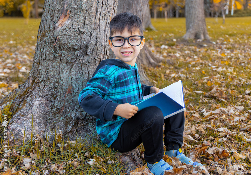 preschooler boy with glasses frame reading a book in park,leaning ...