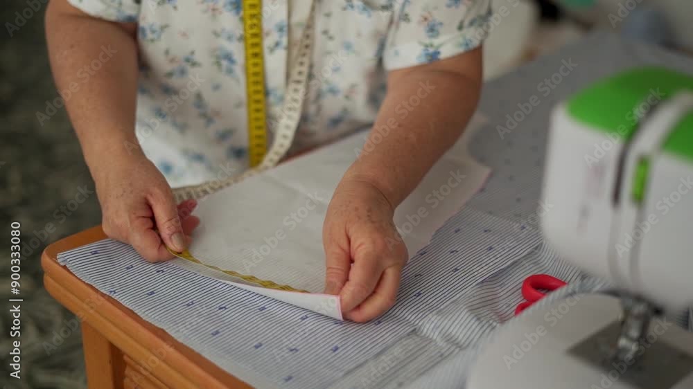 senior woman measuring a sewing pattern on fabric using a tape measure ...