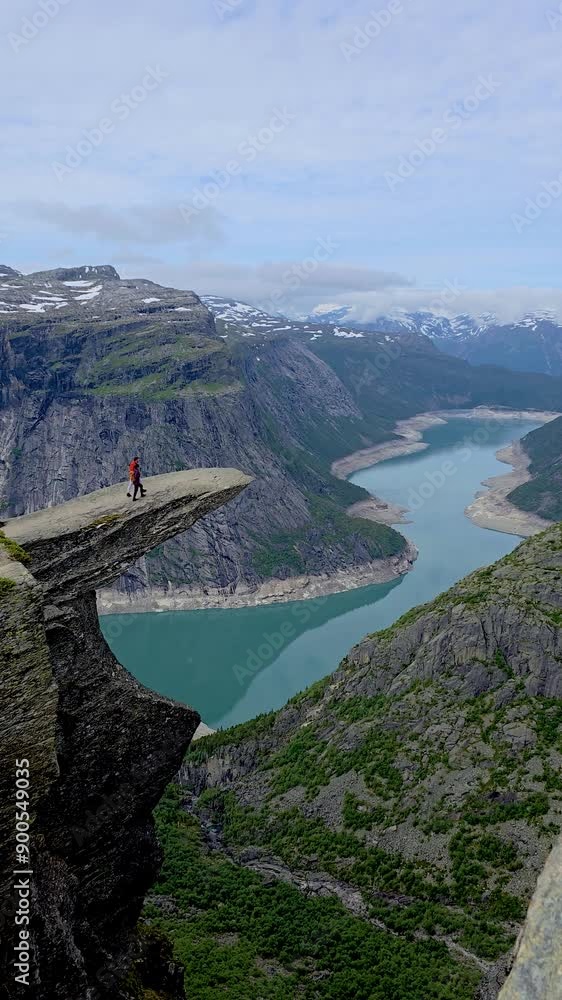 two individuals at the edge of a cliff, gazing at a lovely lake. The ...