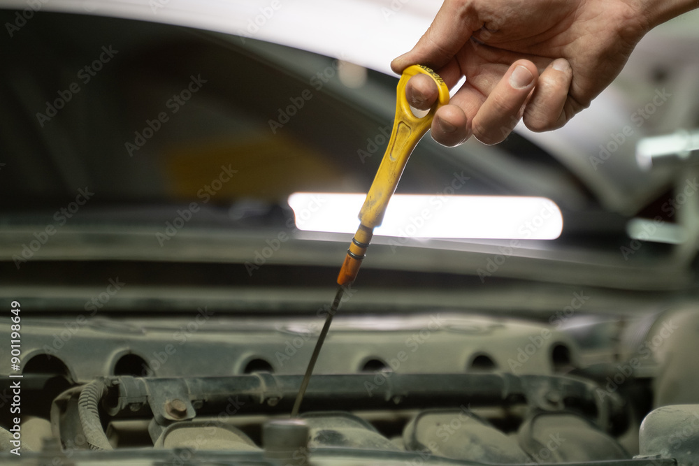 A hand holds a yellow dipstick and inserts it into a car engine to ...