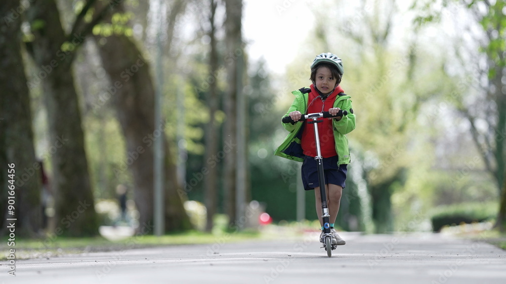 Young child riding a scooter on park path, wearing green jacket and ...