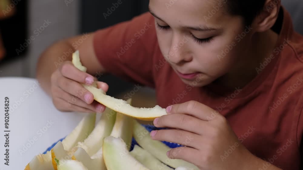 A young boy takes a bite of melon, displaying a thoughtful expression ...
