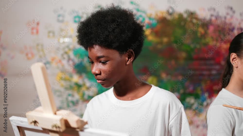 Smart african boy painting canvas while cute girl drawing behind. in ...