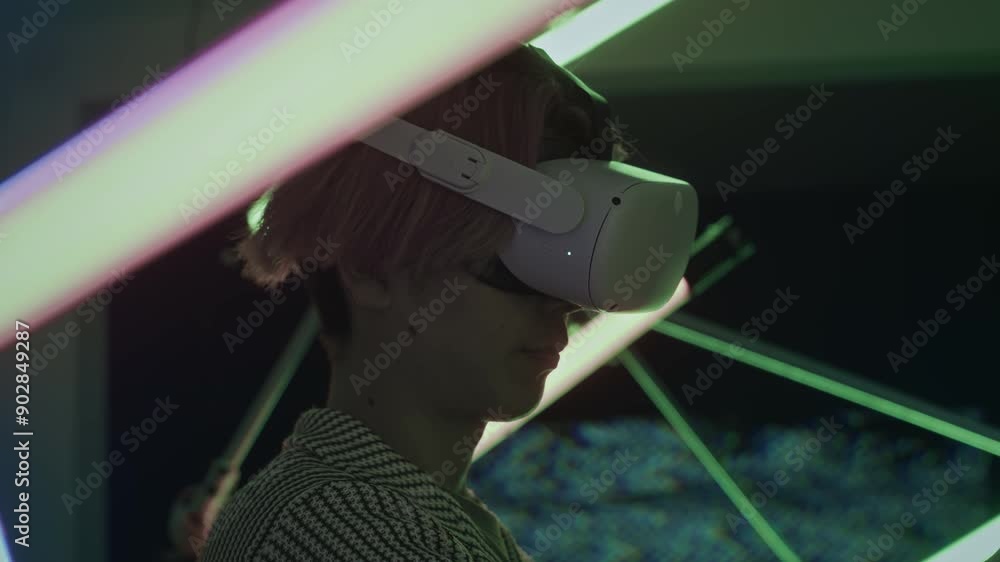 Young man in VR glasses standing among neon lamps in dark room and ...
