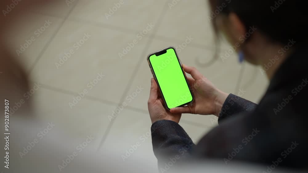 Over-the-shoulder shot. A woman in a blazer is holding a cell phone ...