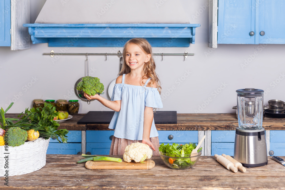 Cute little girl holding broccoli while standing in modern kitchen ...