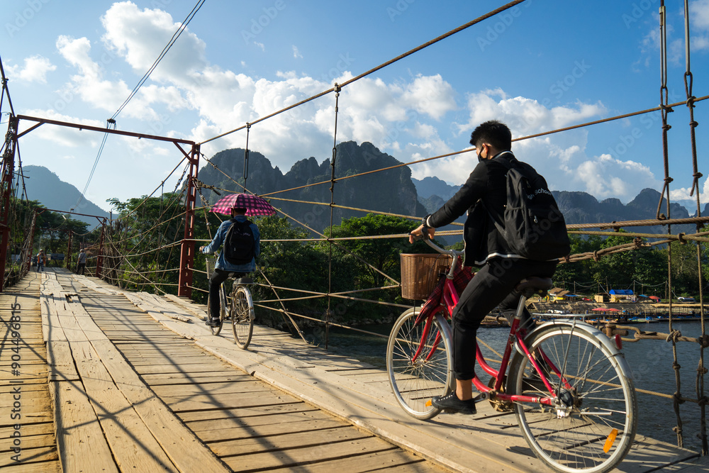 Young men crossing a wooden bridge over Nam Song river on their bicycle ...