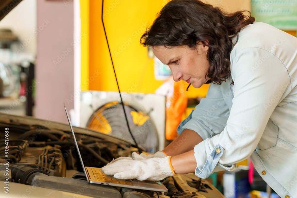 Caucasian woman adult mechanic analyzing data on laptop over car engine ...
