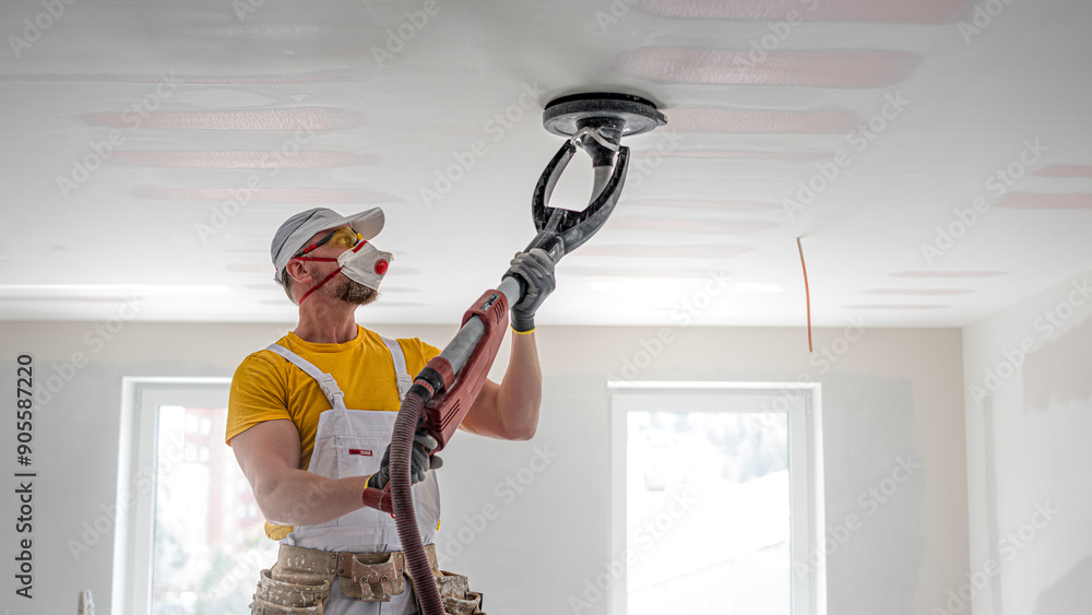 The worker sanding a plasterboard ceiling. He is using special drywall ...