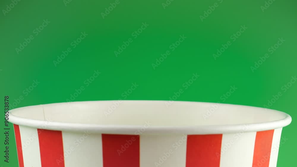Popcorn grains falling into red and white striped bucket isolated on ...