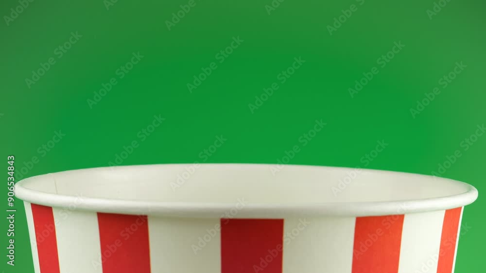 Popcorn grains falling into red and white striped bucket isolated on ...
