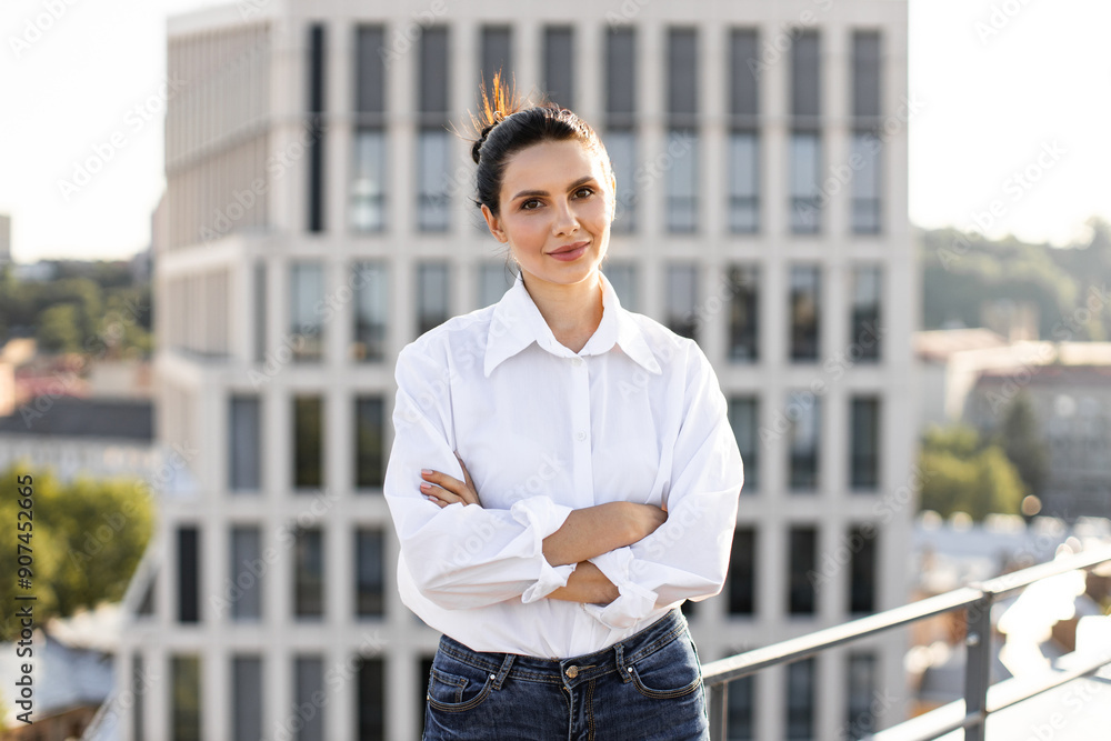 Confident woman standing on rooftop with arms crossed, wearing white ...