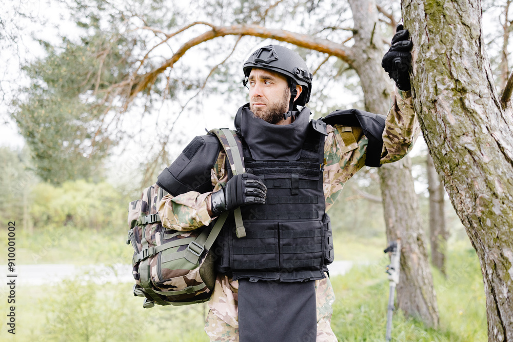 Young soldier in uniforms and tactical vest works in the forest and ...
