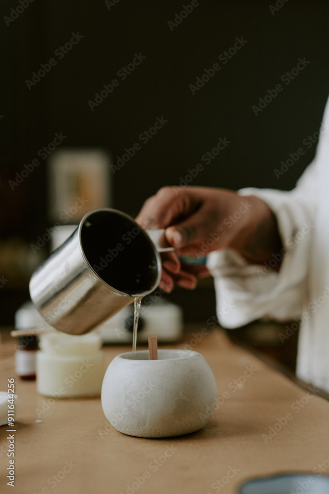 Person pouring wax from a metal container into a stone candle mold, crafting homemade candles in ...