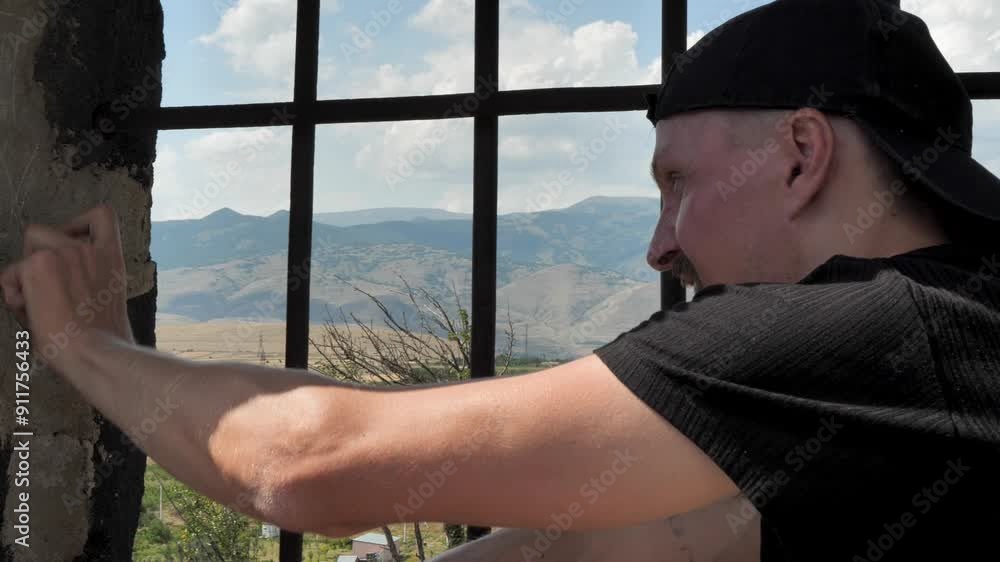 young caucasian male prisoner in prison uses a rock to create writing ...