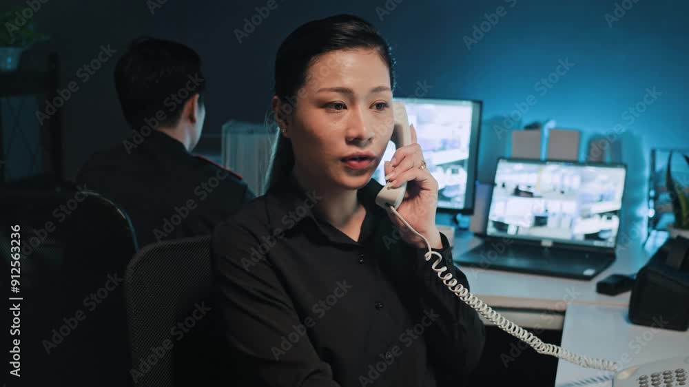 Tilt up shot of female Asian security guard talking on landline phone ...