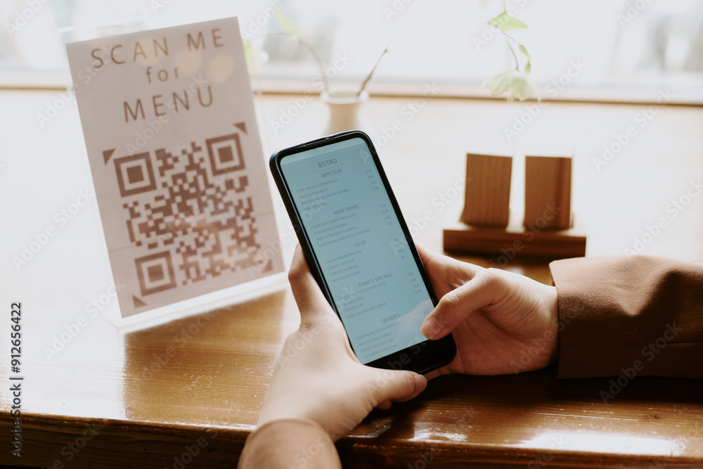 Foto de Person scanning menu QR code with smartphone in cozy restaurant ...